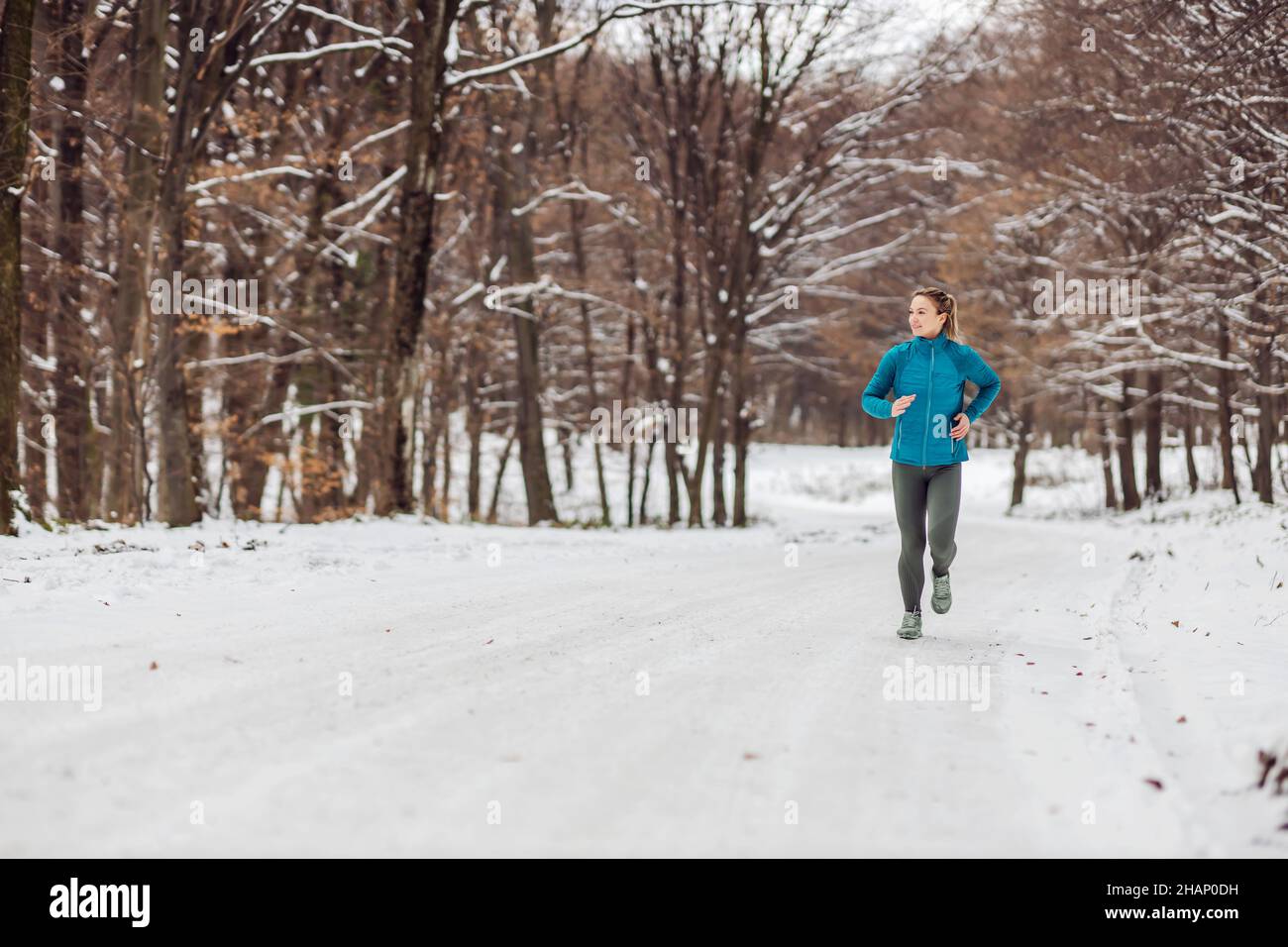 Slim sportswoman jogging in nature on a snowy weather. Cold weather ...
