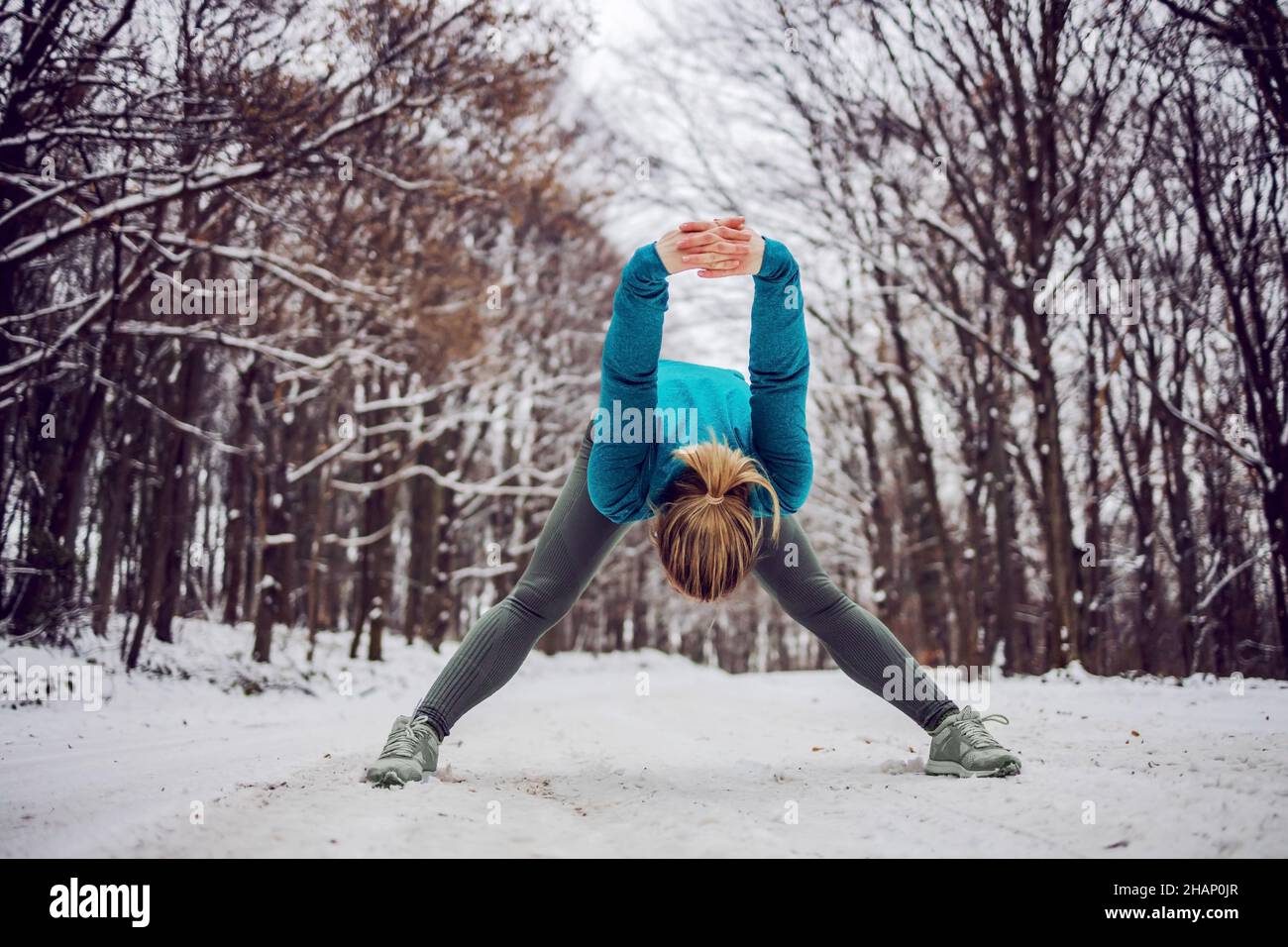 Fit sportswoman standing in snow in forest and doing fitness exercises ...