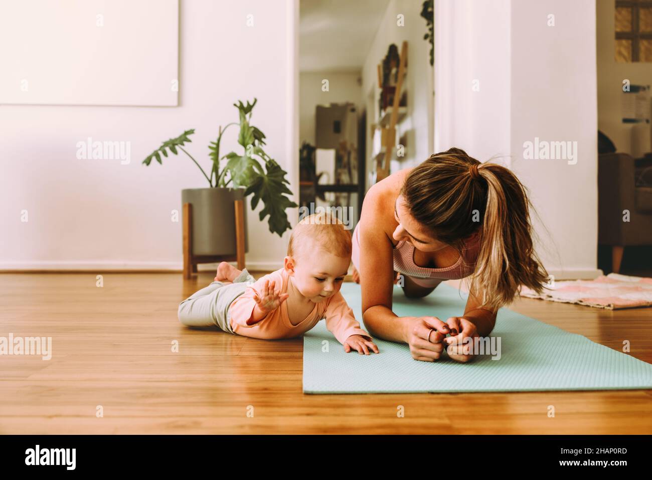 Young mom doing plank exercises with her baby at home. Healthy mom working out with her baby on ...