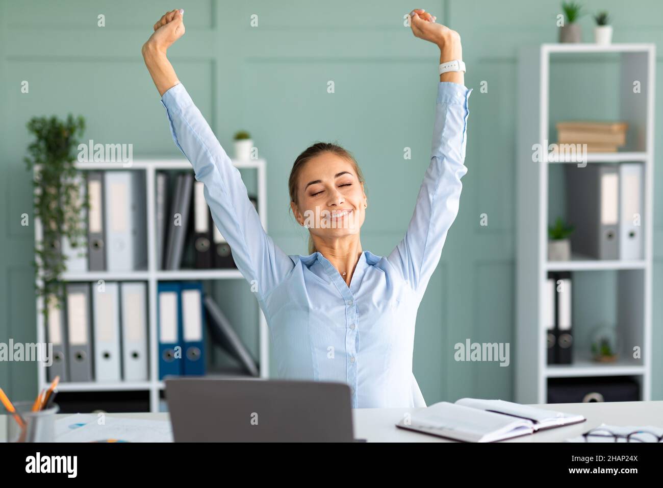 Stress relief. Female office worker stretching hands with closed eyes ...
