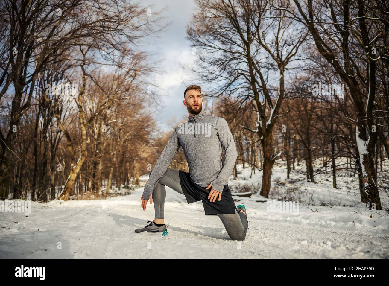 Fit sportsman doing warm up and stretching exercises while kneeling in ...
