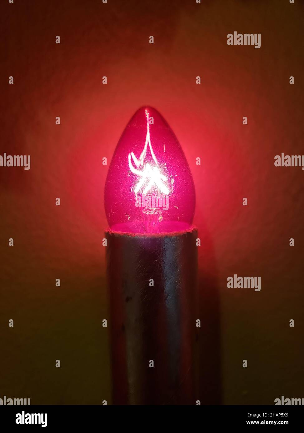 Small red light holiday light bulb against a wall Stock Photo - Alamy