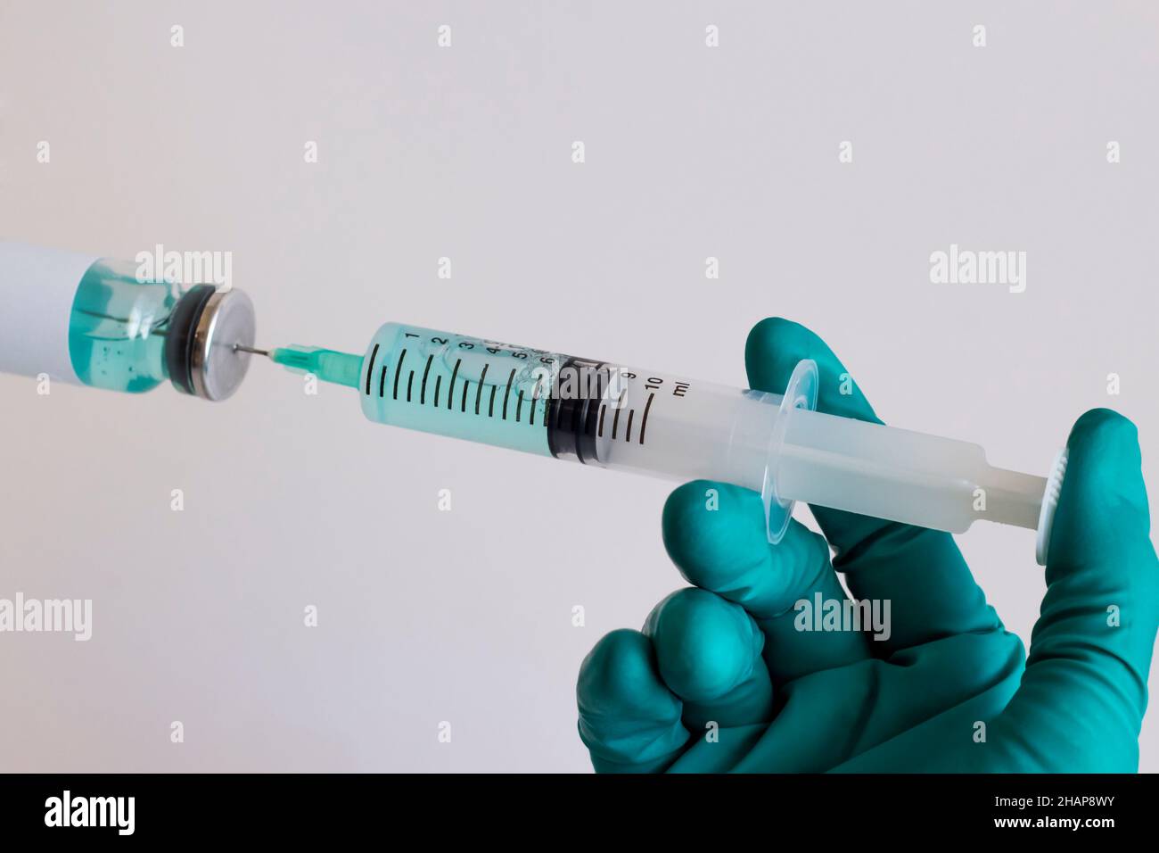 Gloved hand holding syringe,push needle into drug glass bottle on white ...