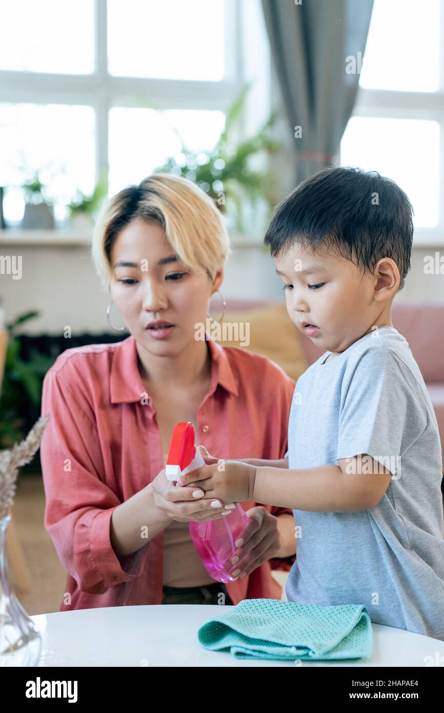 Cute little boy helping his mother with domestic chores while spraying ...