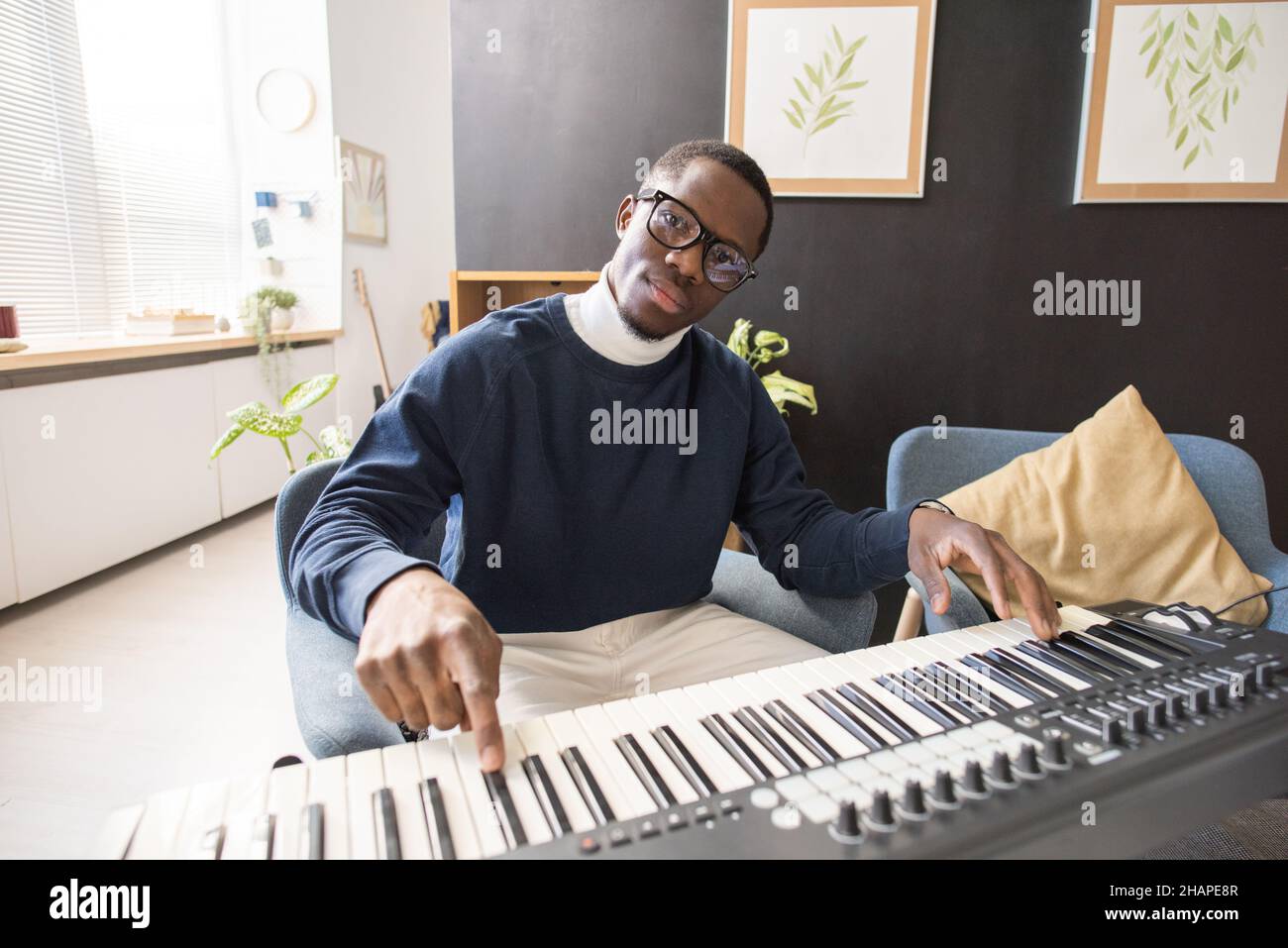 Young serious African man looking at you while pressing key of music ...