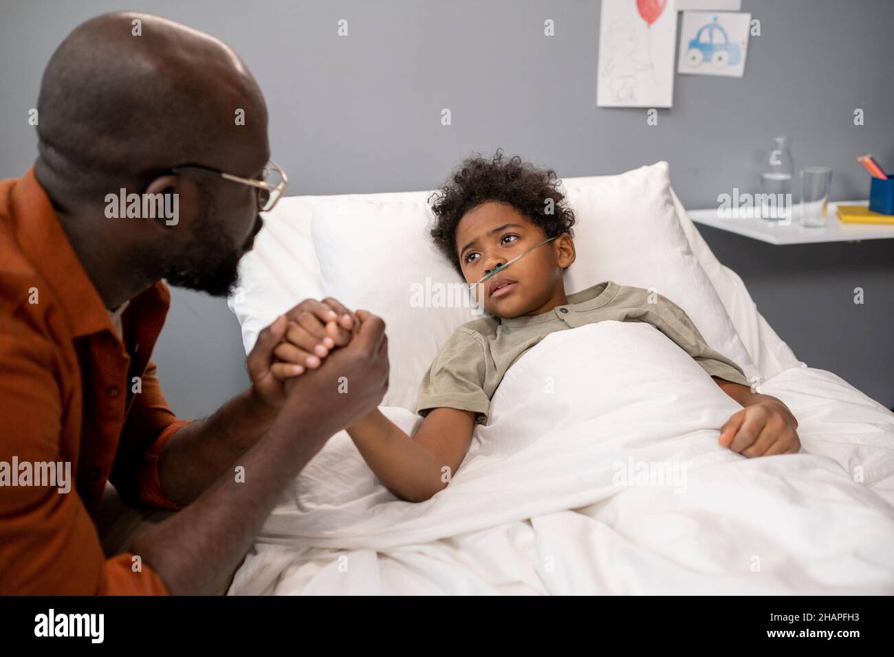 African father holding hand of his son and talking to him during his ...