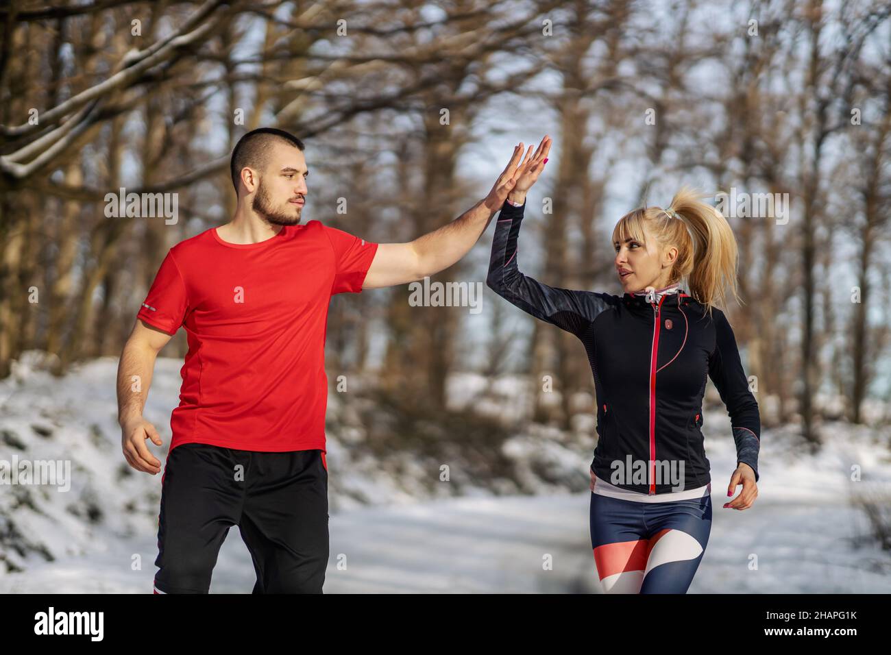 Sporty couple running together on the snow in nature at winter and ...