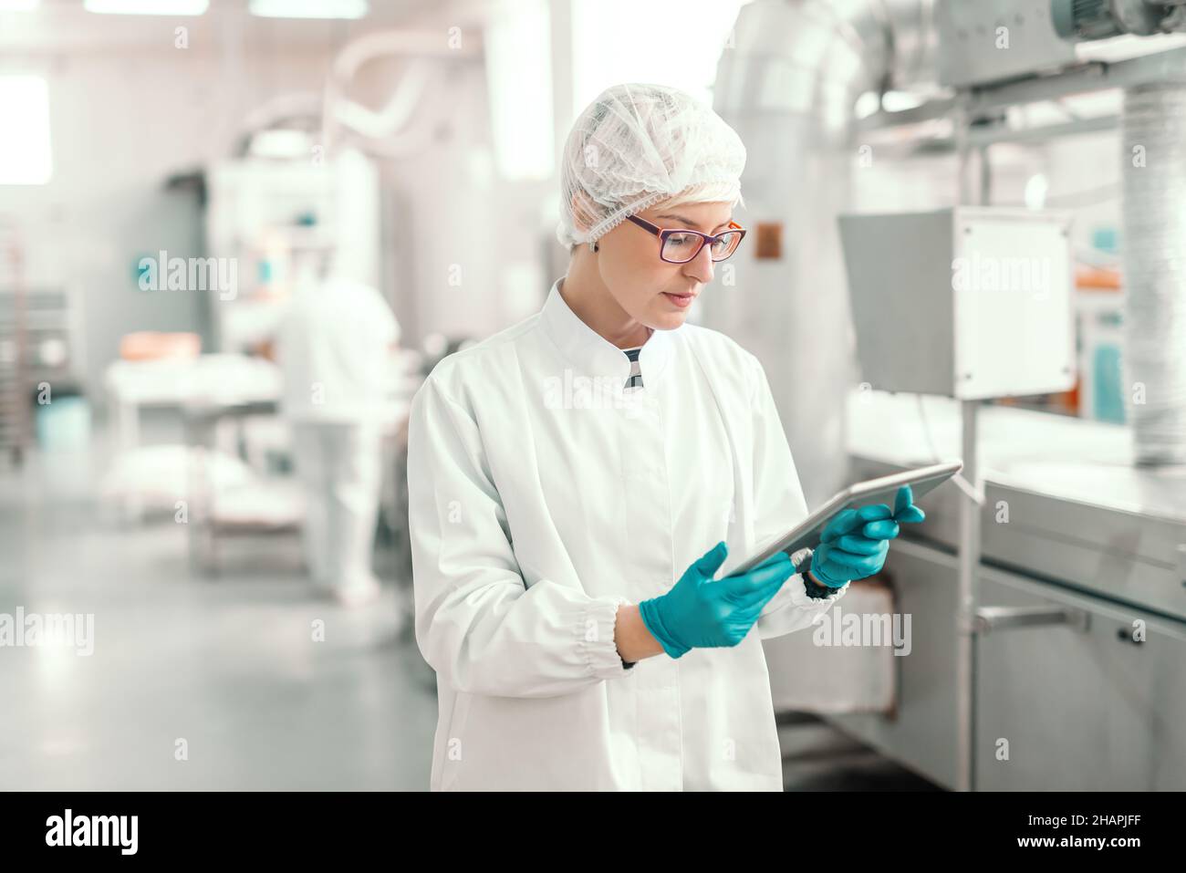 Supervisor in sterile uniform and with eyeglasses using tablet for ...