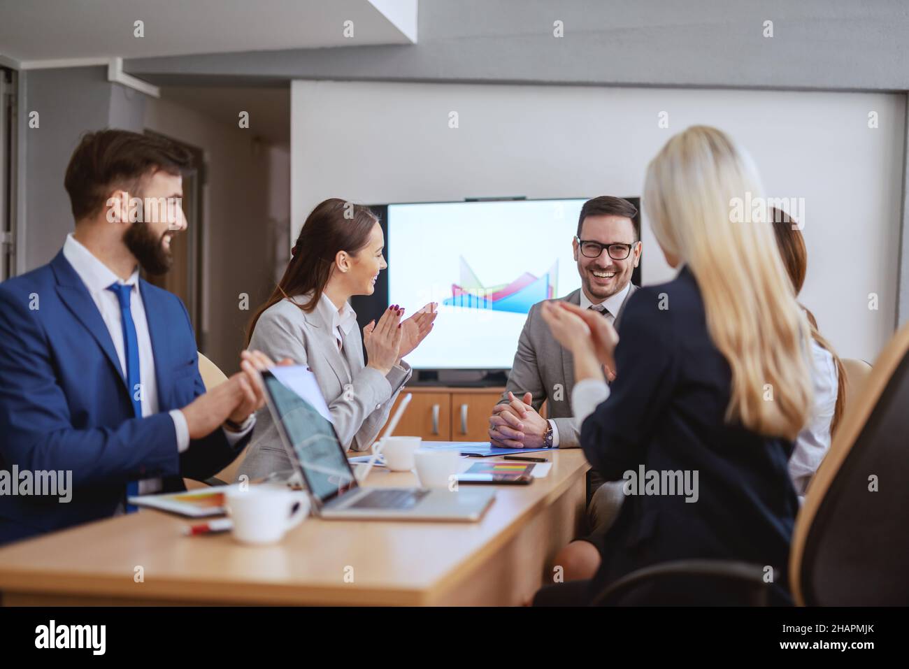 Smiling CEO sitting in boardroom with his team. Team clapping to him. A ...