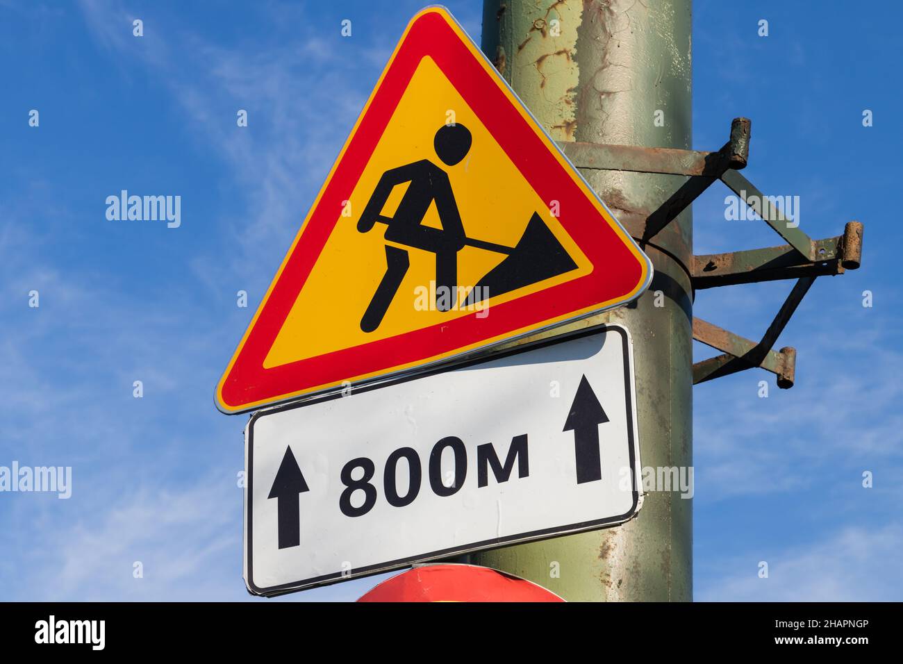 Men at work, road under construction. Road sign mounted on green pillar ...