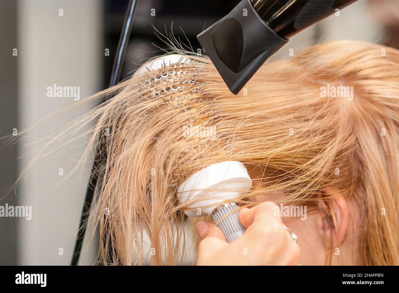 Hairdresser hand drying blond hair with a hairdryer and round brush in ...