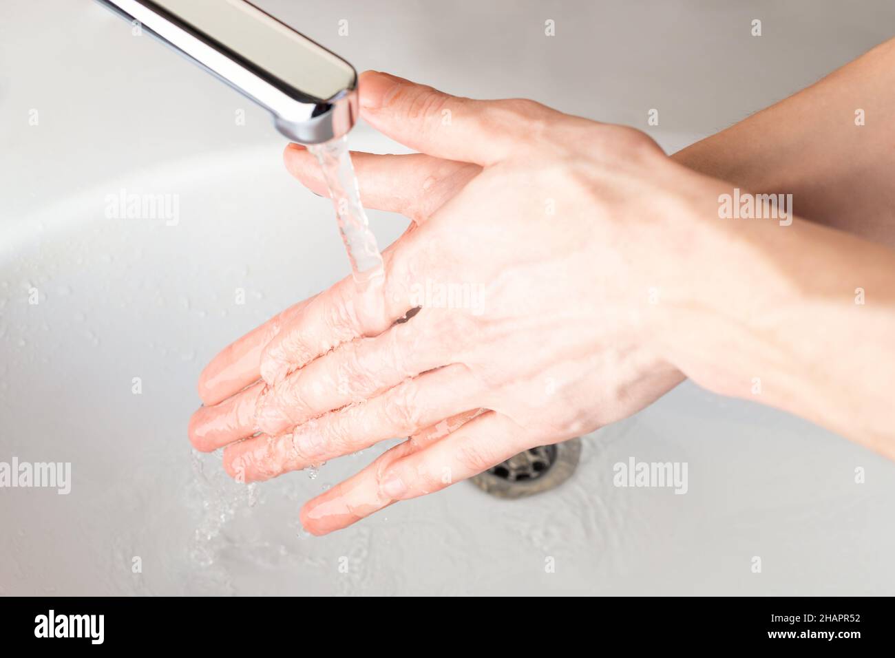 Washing hands under a stream of water in the bathroom over the sink ...