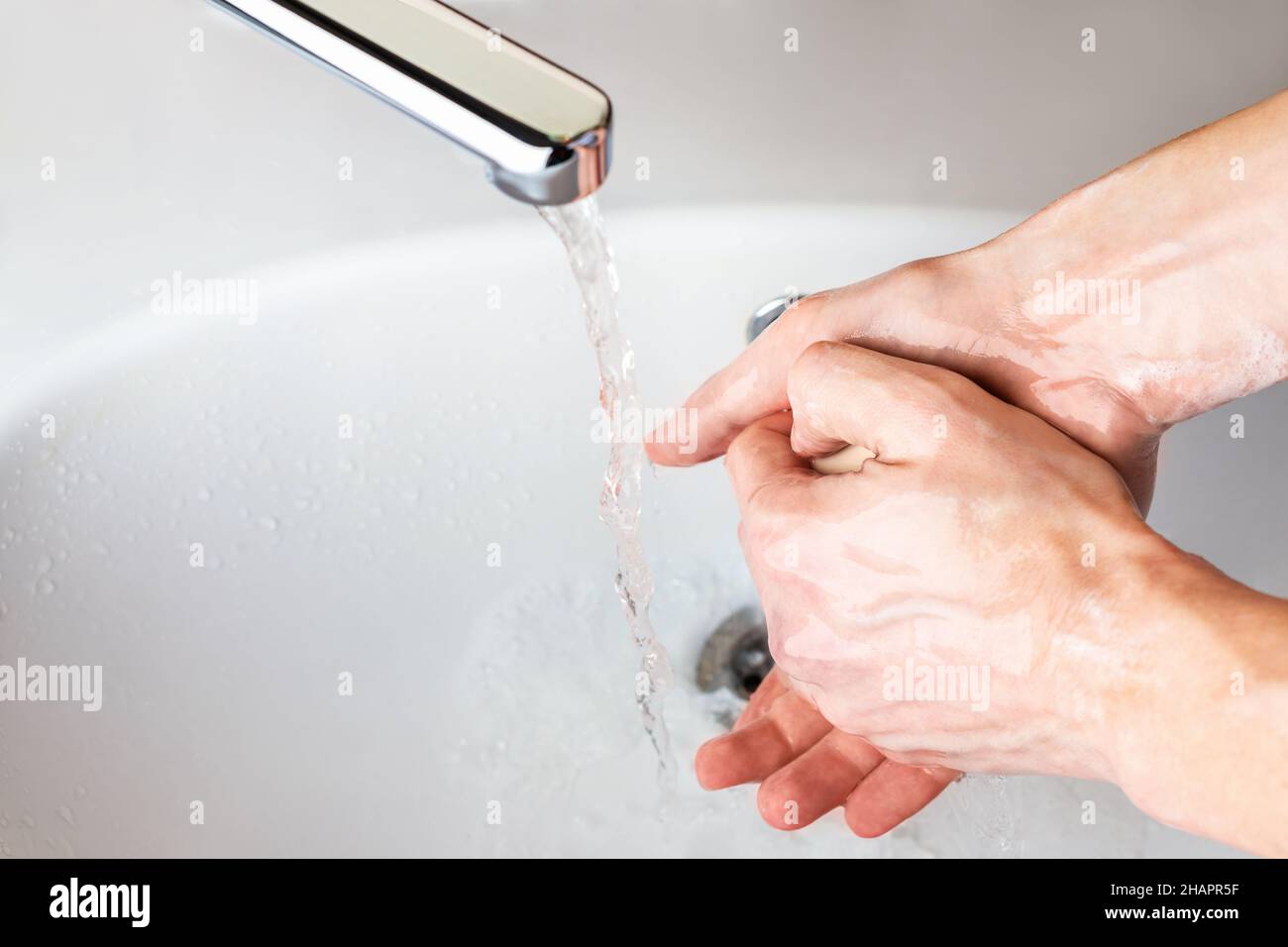 Washing hands with soap under a stream of water in the bathroom over ...