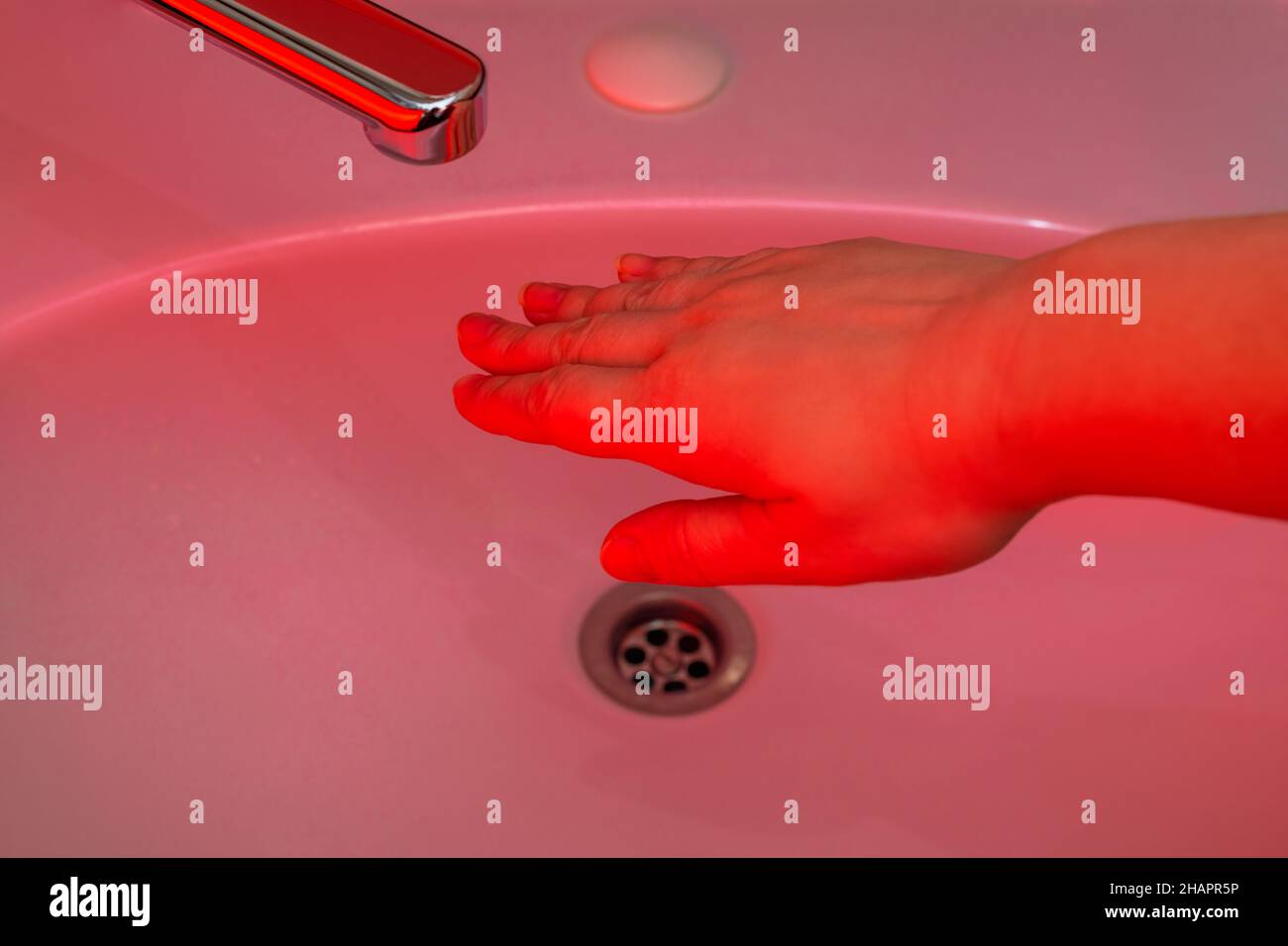 One hand reaches for the red-lit water tap. Hygiene concept for ...