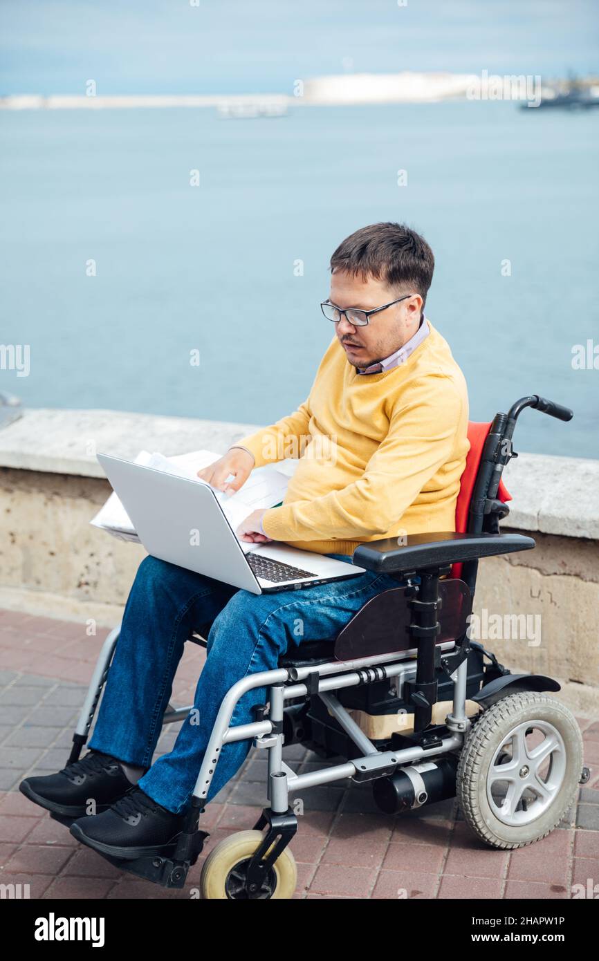 a man with disabilities in a wheelchair works on a computer on the ...