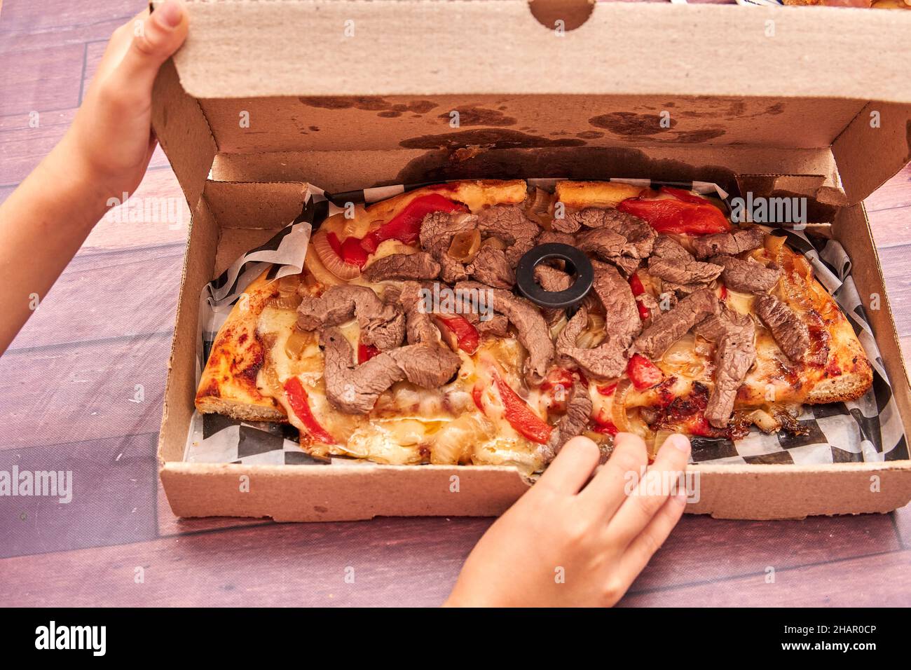 A child's hands opening a pizza cardboard box with sliced meat, melted ...