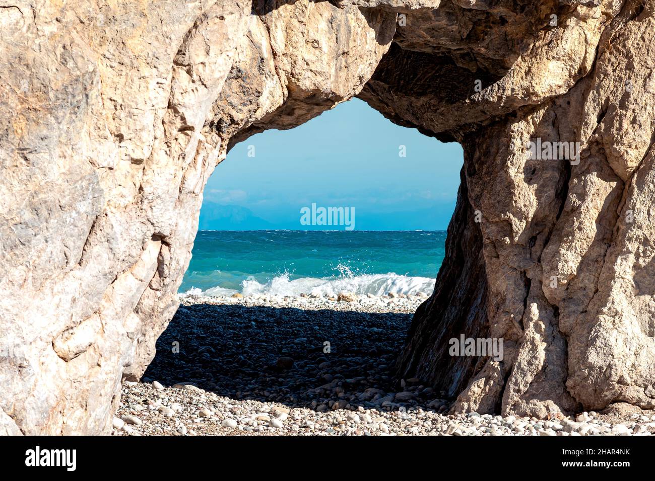 natural stone arch on the seashore, behind which sea surf can be seen ...