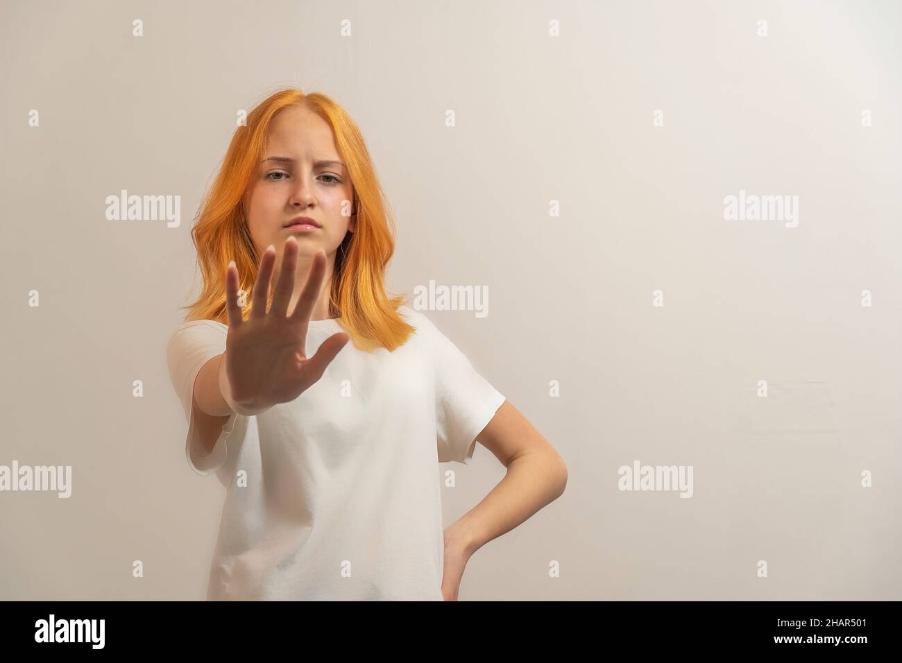 teen girl with red hair in a white t-shirt on a light background denial ...