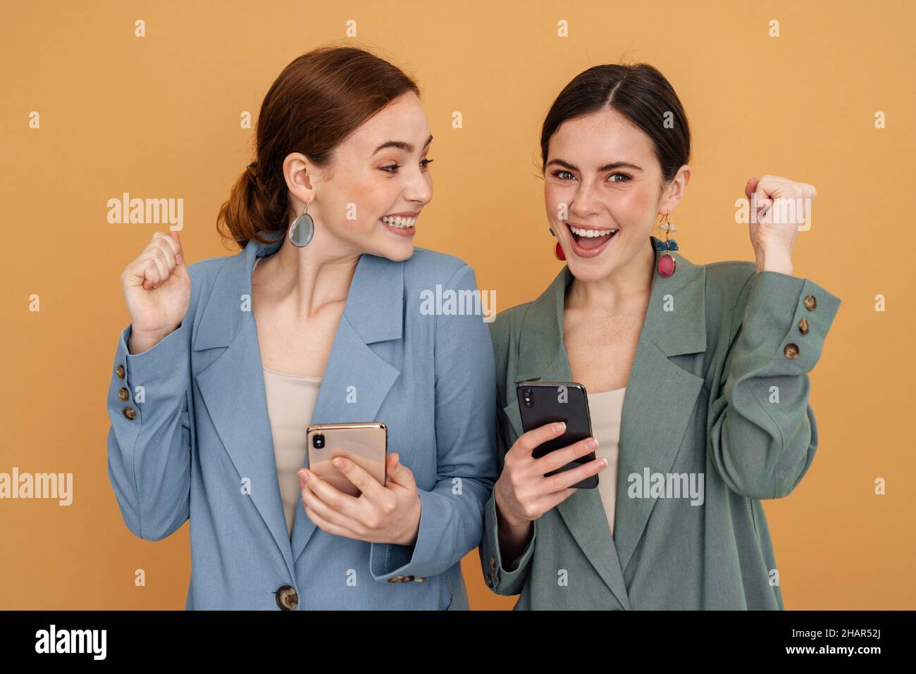 Young two women using mobile phones and making winner gesture isolated ...
