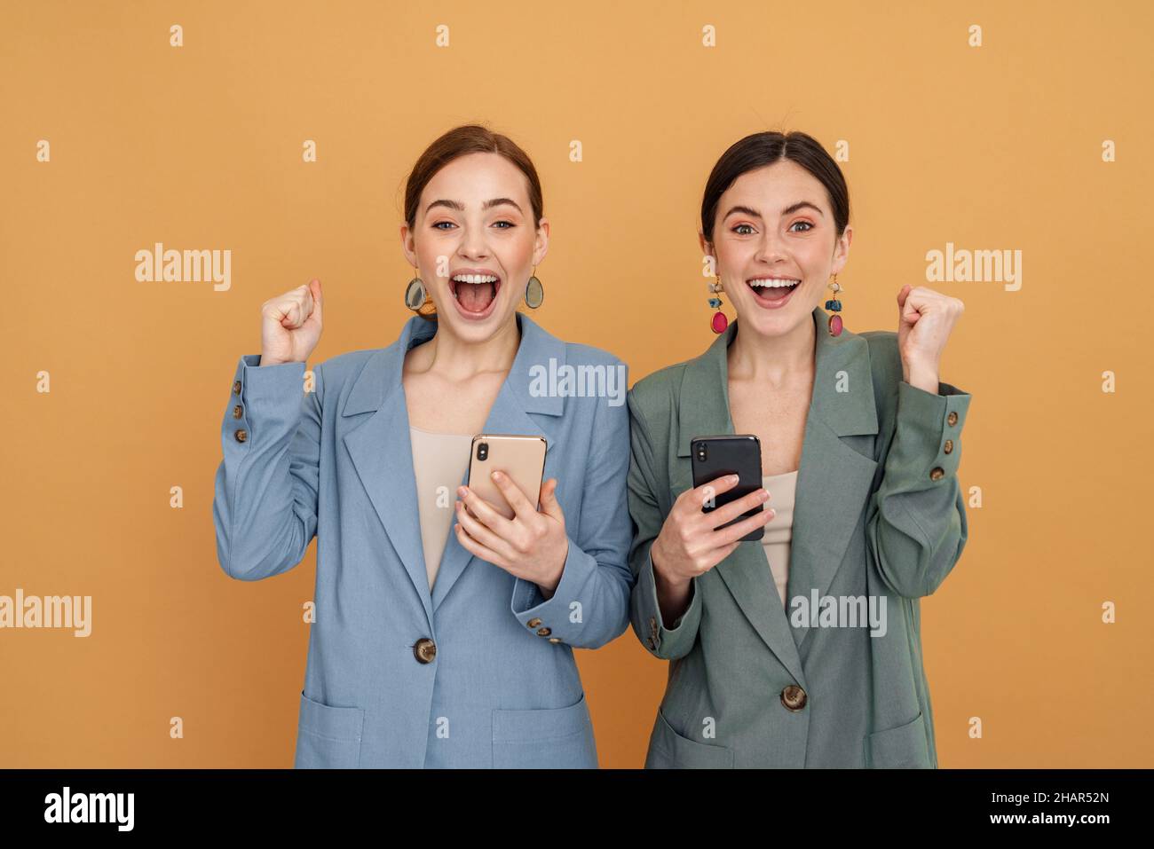 Young two women using mobile phones and making winner gesture isolated ...