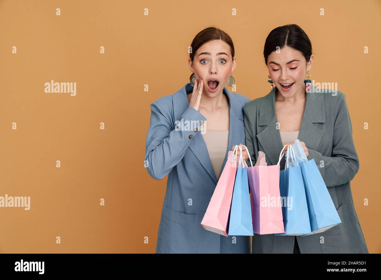 Young two women holding shopping bags and expressing surprise isolated ...