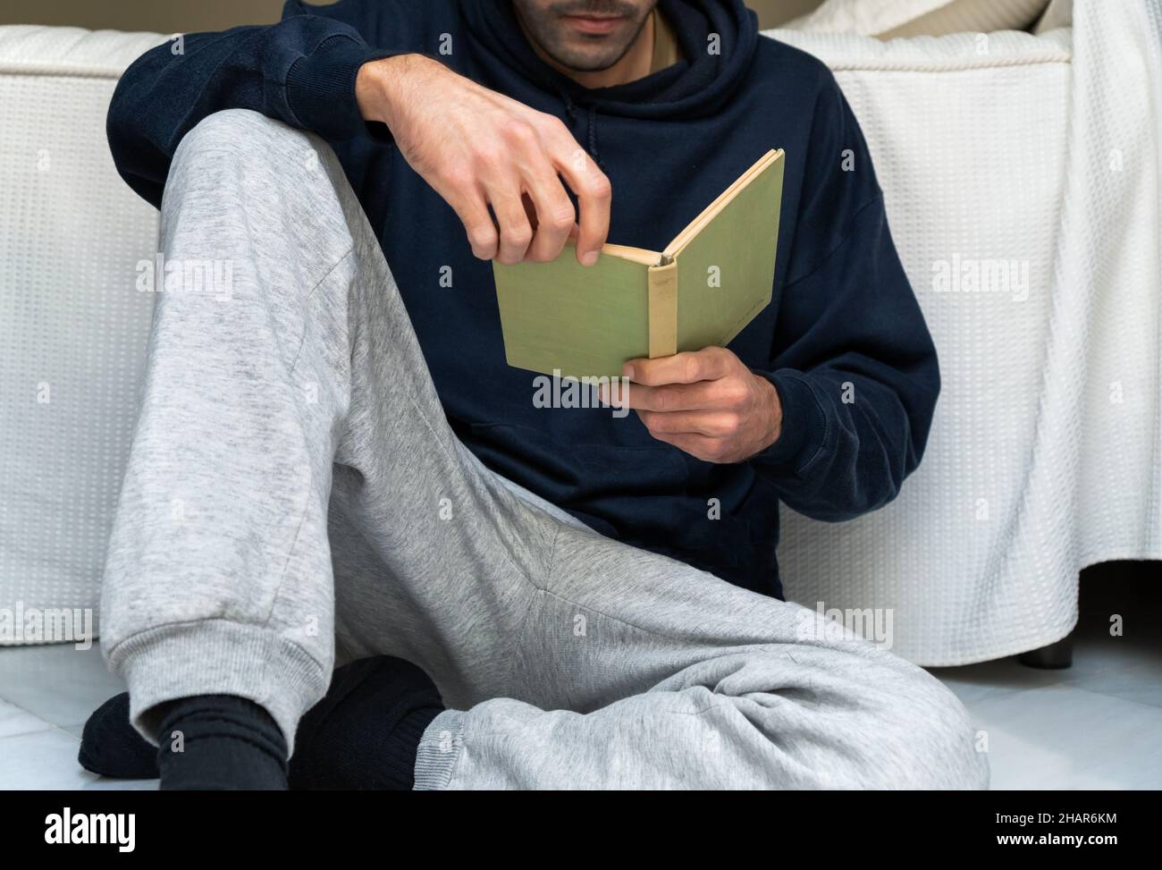 Young man in comfortable clothes reading book next to the bed at home ...