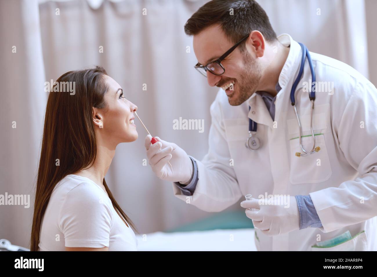 Smiling Caucasian doctor taking swab from his patient's nose. Clinic ...
