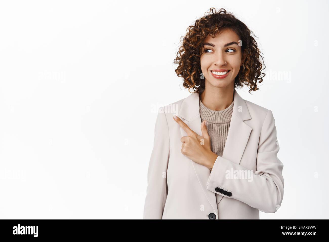 Smiling office lady in suit, looking and pointing left at left side ...