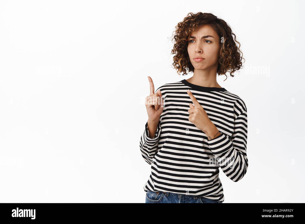 Disappointed young woman with concerned face, pointing and looking left ...