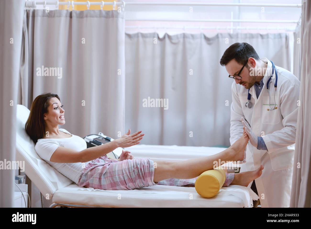 Male doctor in white uniform examining leg injury. Patient lying down ...