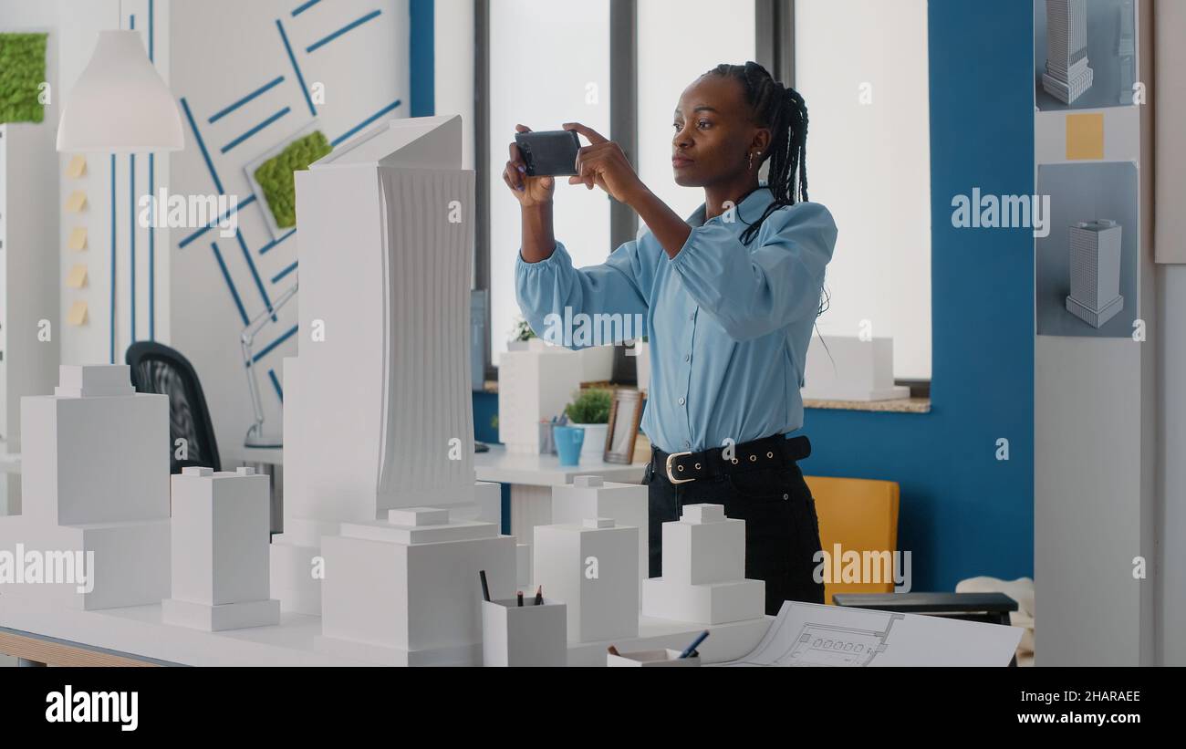 Woman engineer using smartphone to plan layout of building model and ...