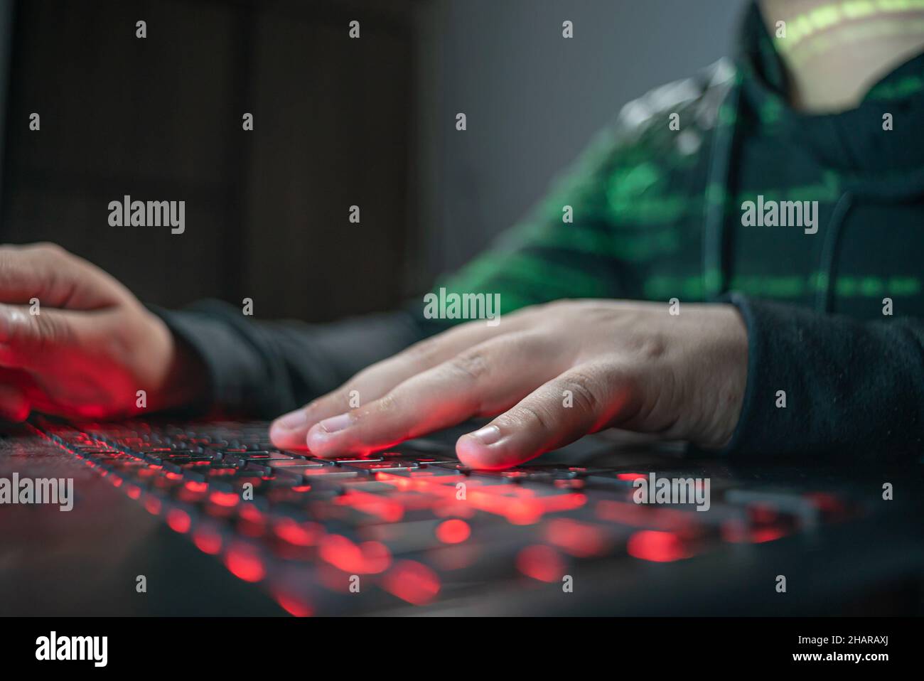 Hispanic man in front of his laptop with green coding lights on him ...
