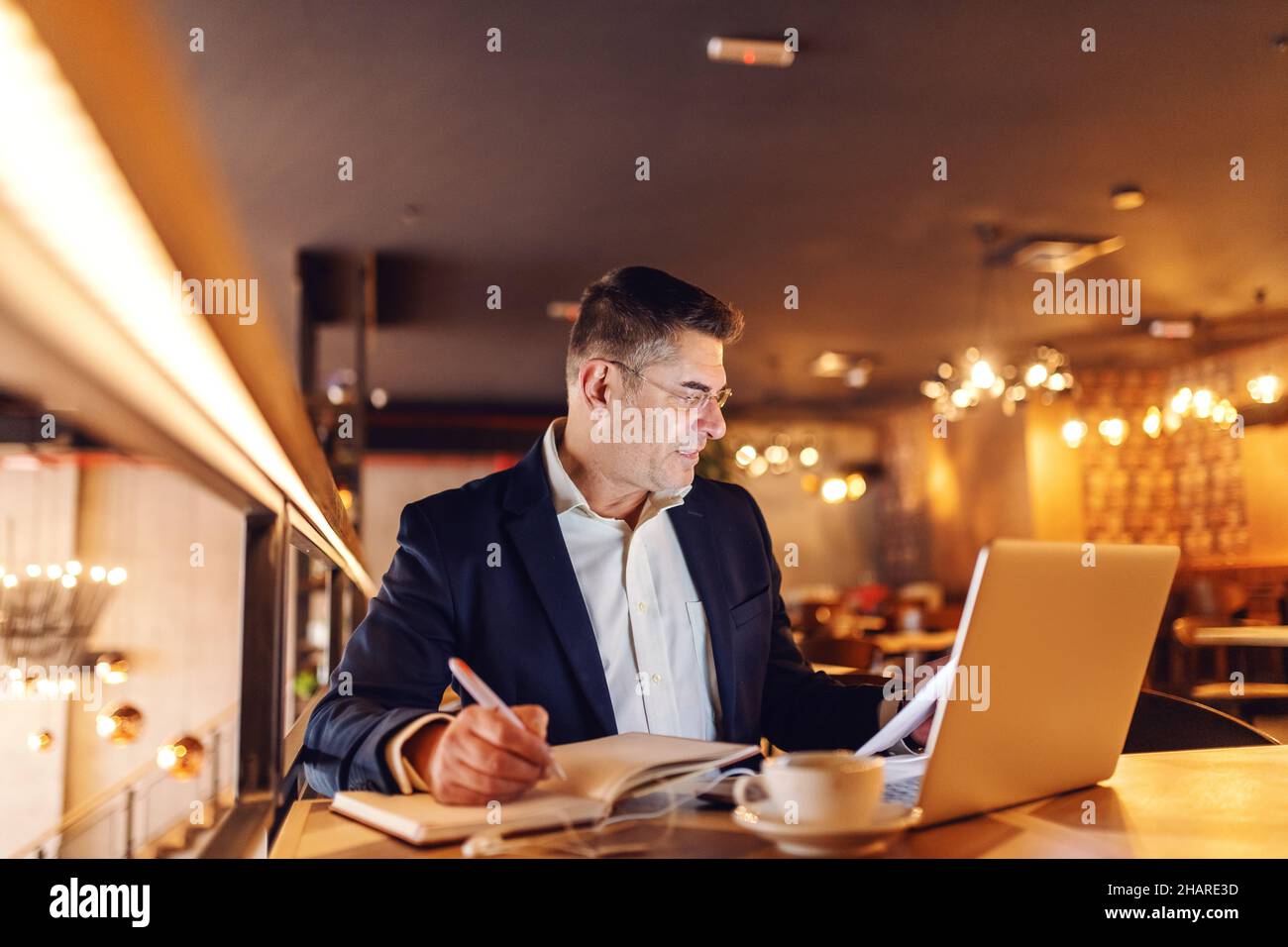 Middle aged CEO dressed smart casual writing in agenda schedule and ...