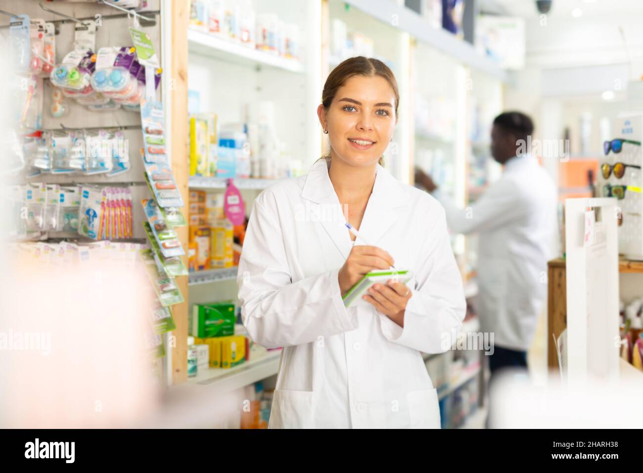 Young smiling female pharmacist making important notes in a notebook ...