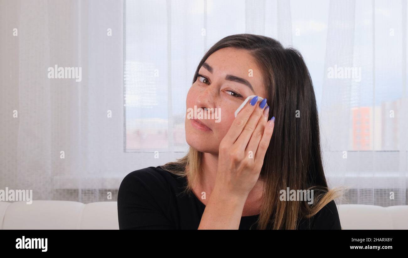 Young girl cleanses her perfect skin with a sponge with a white cotton pad in front of a mirror ...