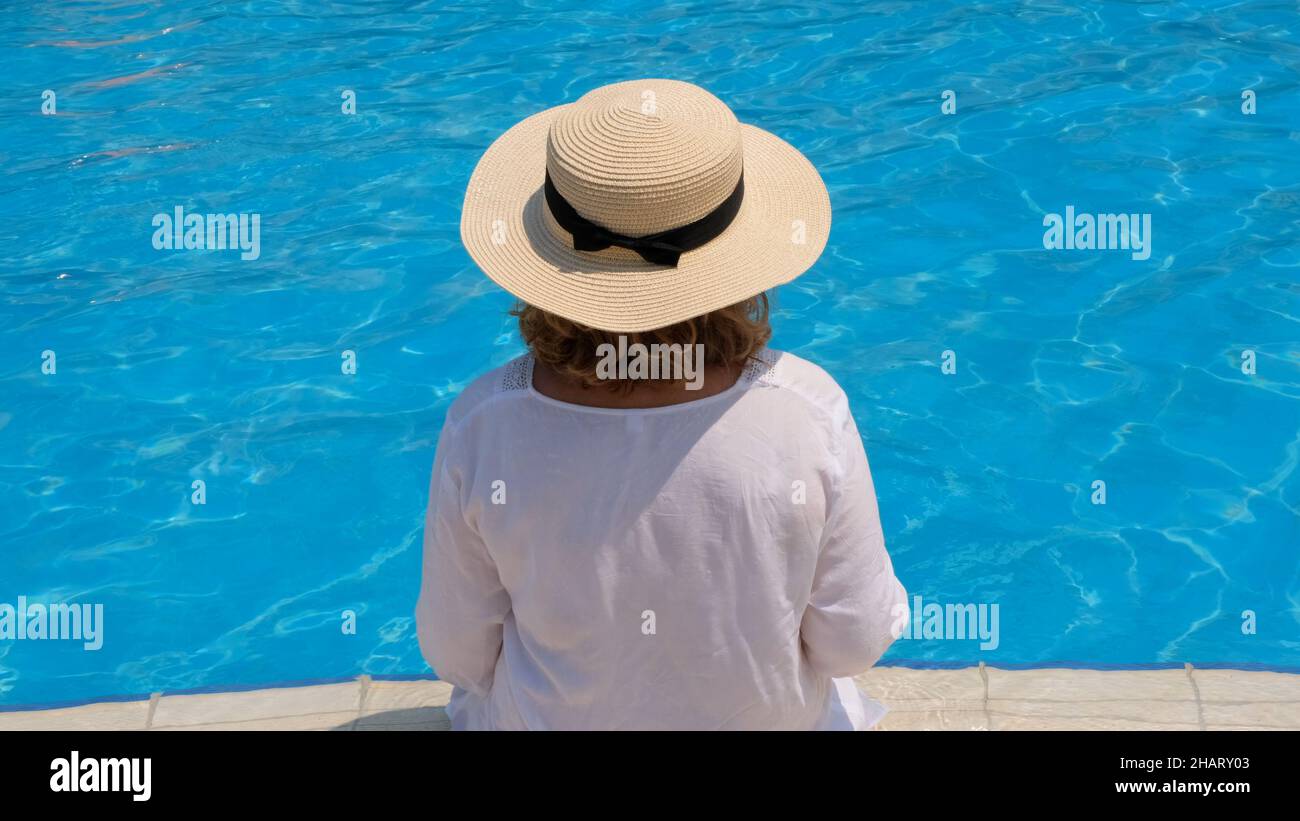 Senior woman relaxing near the hotel's blue outdoor swimming pool ...