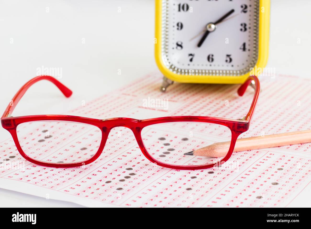 Alarm clock,wooden pencil and glasses on filled exam sheet,conceptual ...