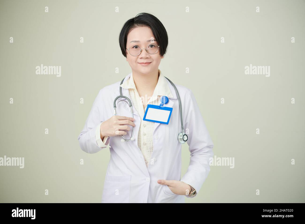 Portrait of positive smiling female general practitioner with badge and ...