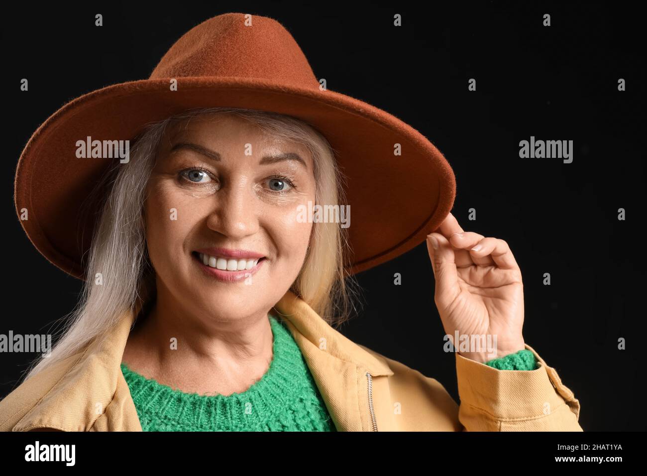 Portrait of fashionable mature woman in felt hat on dark background ...
