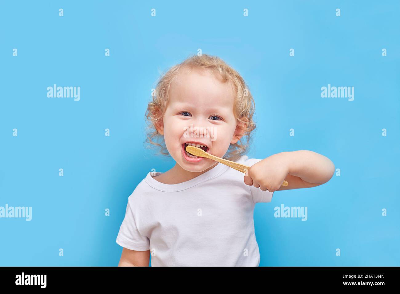 left-handed child brushes his teeth with a bamboo toothbrush on a plain ...
