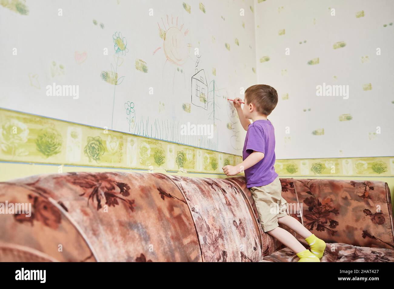 kid draws on the wallpaper standing on the sofa in the living room. The ...