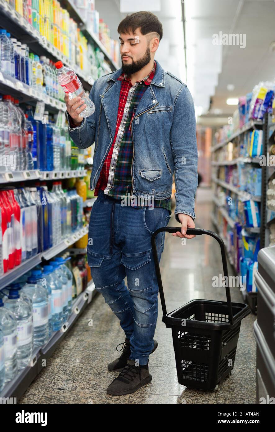 Portrait of focused young man purchasing bottled water in grocery store ...