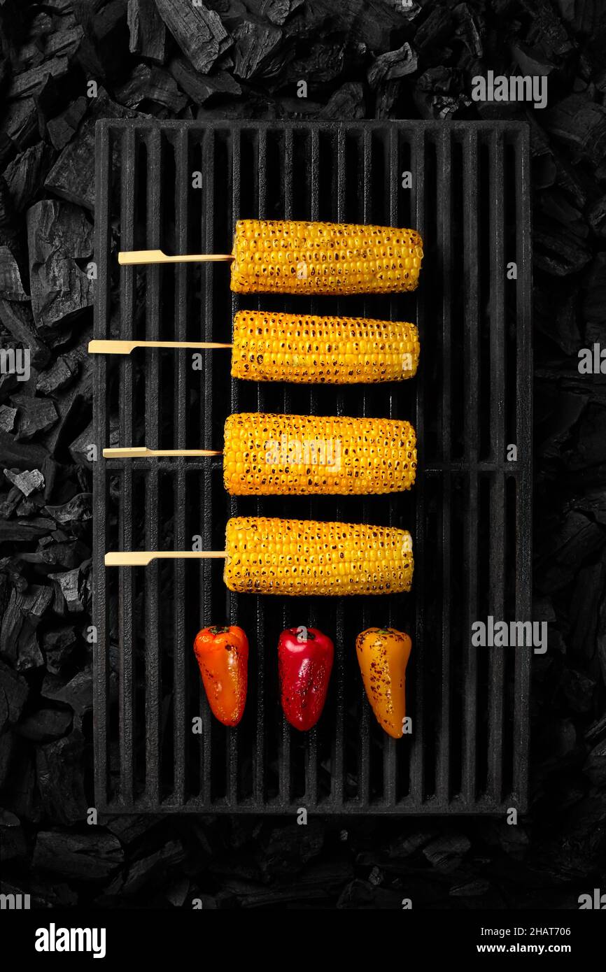 Grilled ears of corn and bell peppers on barbecue grate over cold coals ...