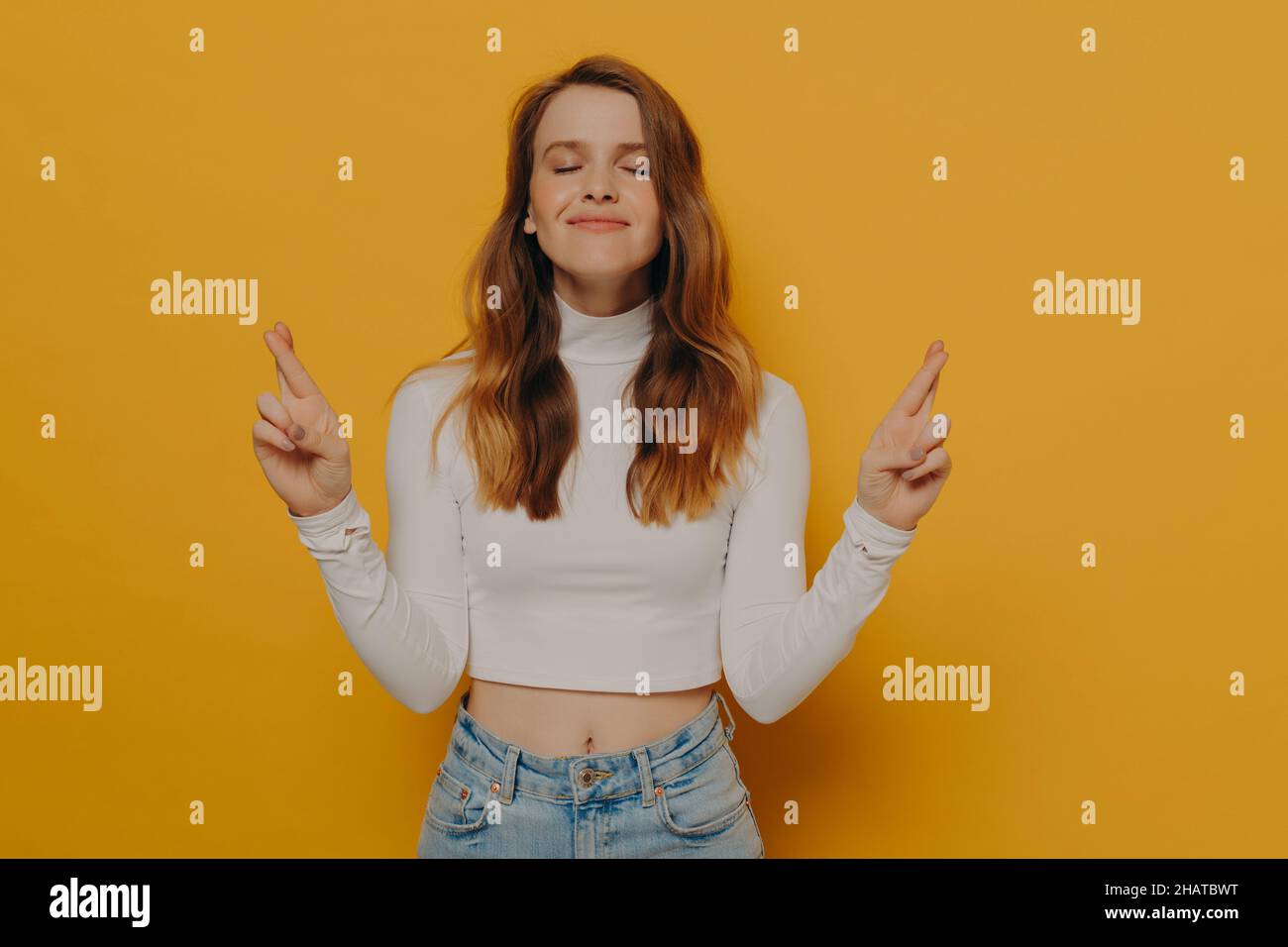 Hopeful woman standing isolated over yellow background with crossed ...