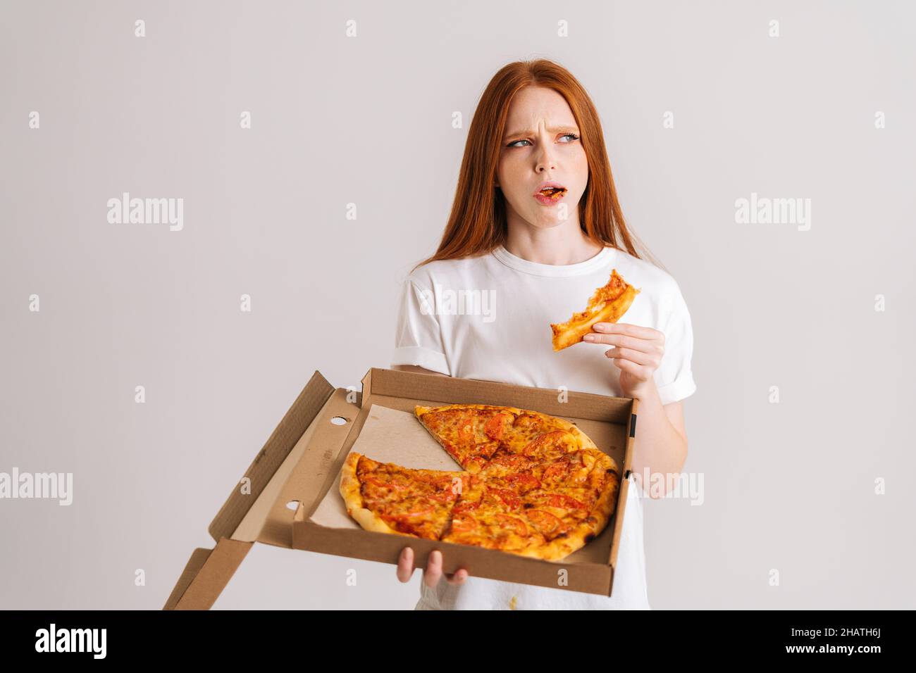 Studio portrait of dissatisfied young woman eating bad quality pizza ...