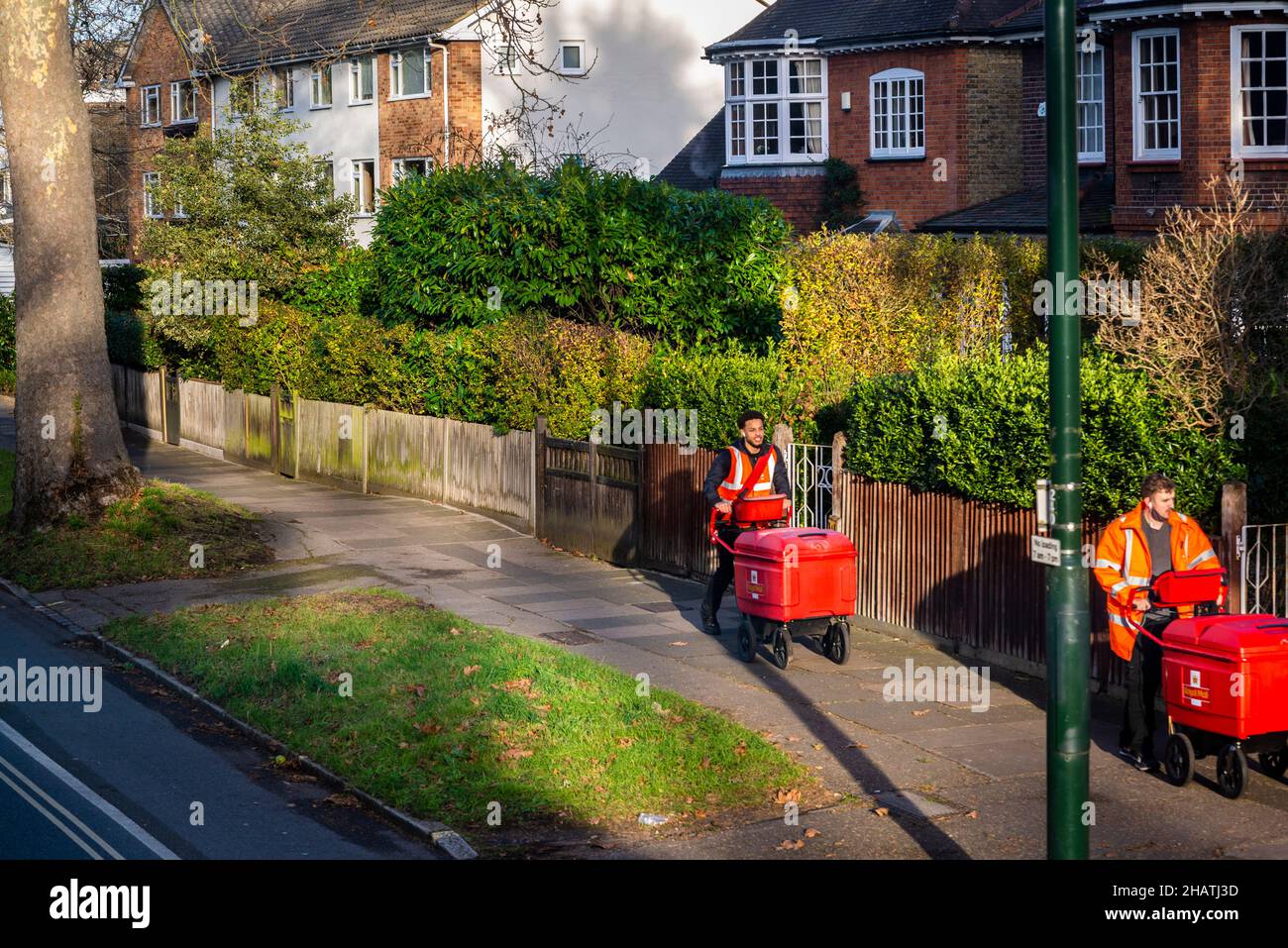 Two postmen pushing their trolleys in a suburban street, London ...