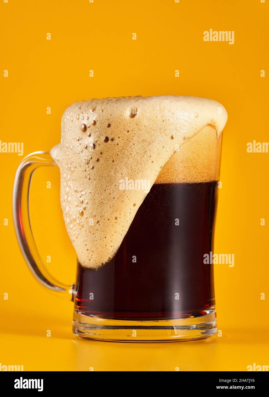 Dark brown beer in a half liter glass mug isolated on yellow background ...