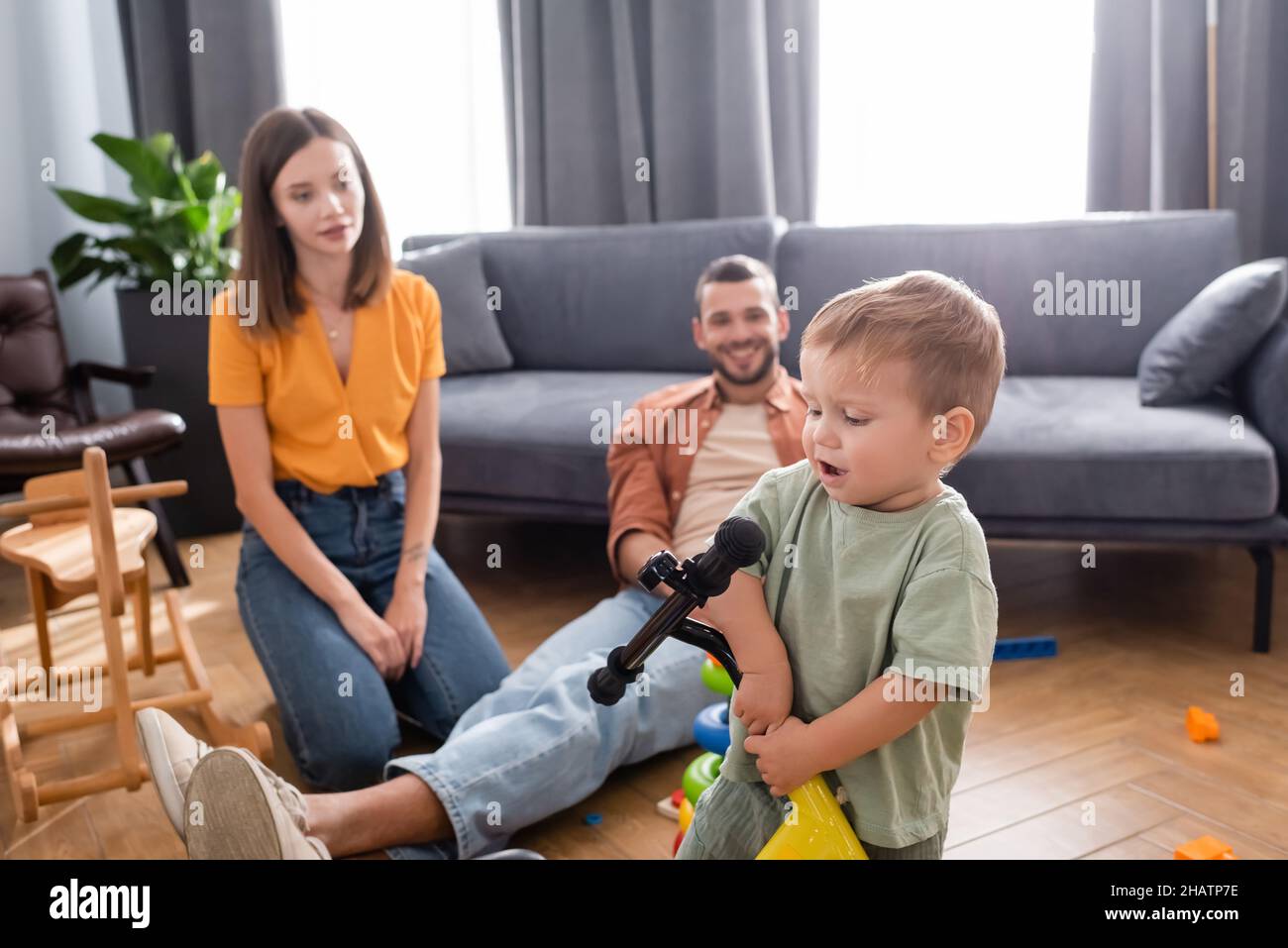 Toddler child holding bike near blurred parents and rocking horse at ...