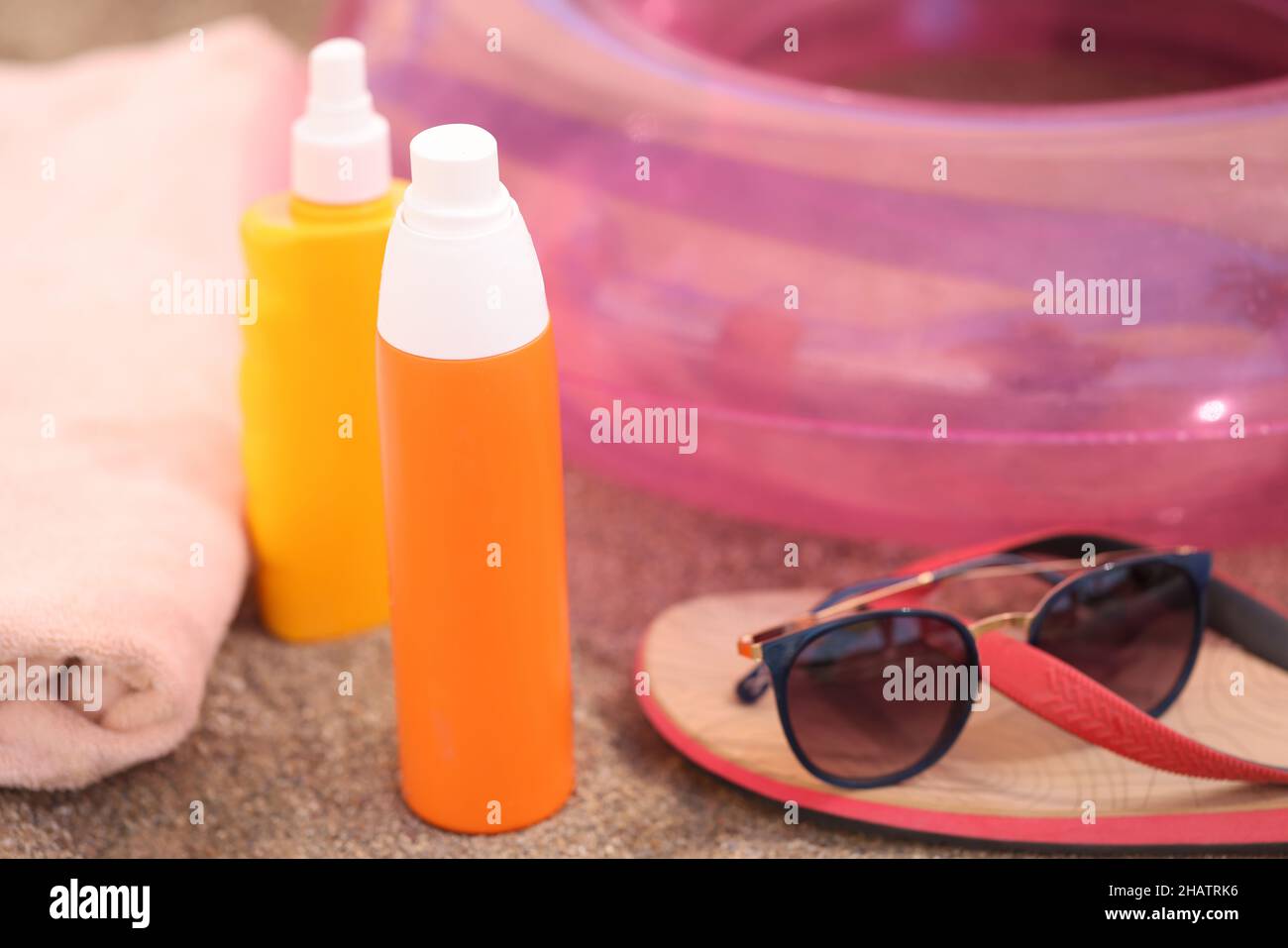 Jars of sunscreen and sunglasses lying on sand near swimming circle ...