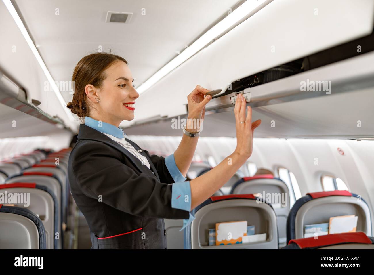 Cheerful flight attendant closing overhead luggage bin in airplane ...